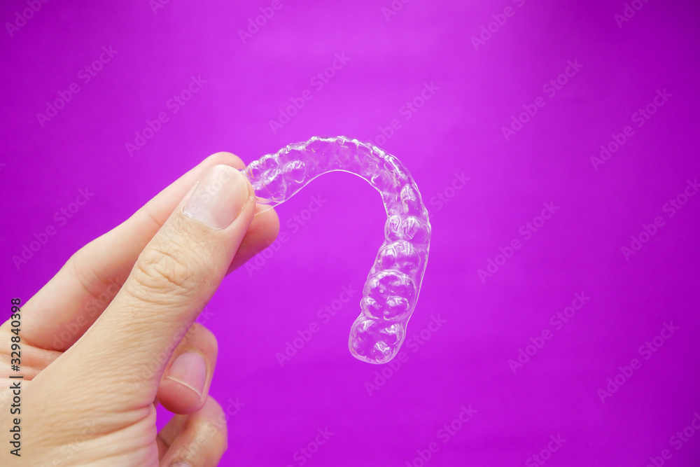 hand holding clear plastic retainer teeth that isolated on purple ...