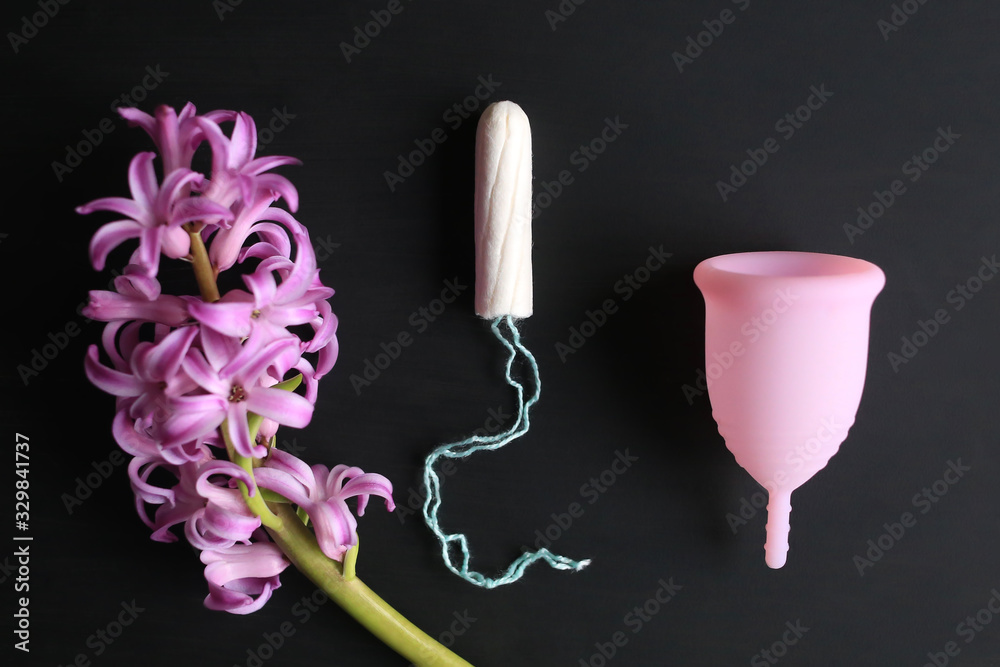 Medical female tampon and menstrual Cup, and flower on black background ...