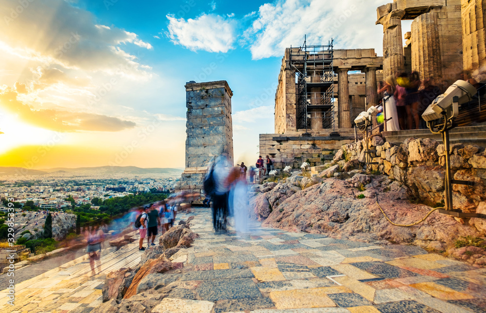 Motion blur image of crowd of tourists walking around in front of the ancient ruins of Parthenon ...