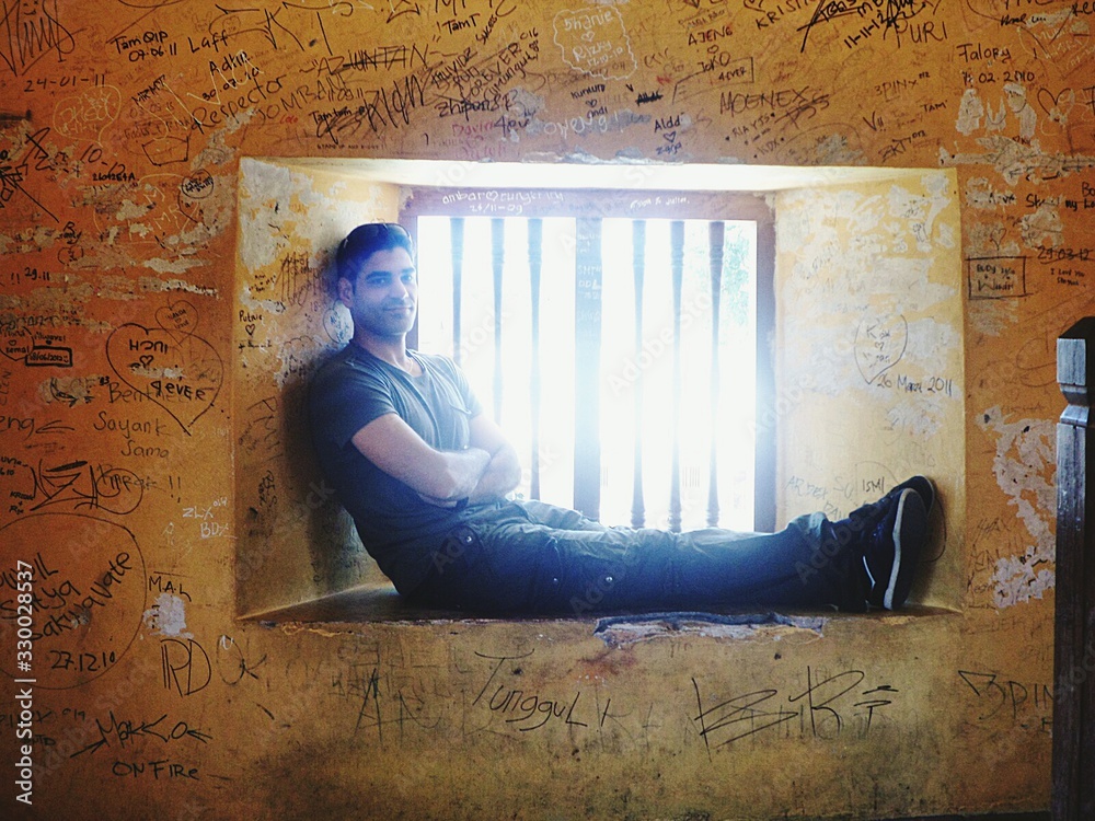 Full Length Portrait Of Man Sitting On Window With Text On Wall Stock ...