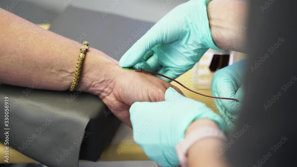 Phlebotomist technician drawing blood from arm of a patient with needle ...