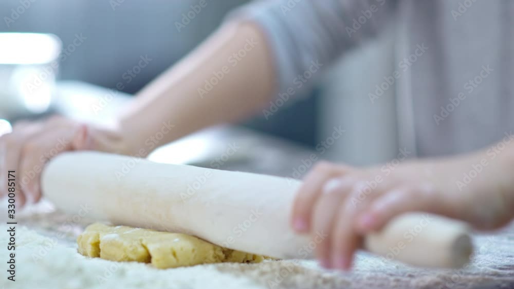 Child hands rolling dough with a rolling pin, macro. Boy rolls out the ...