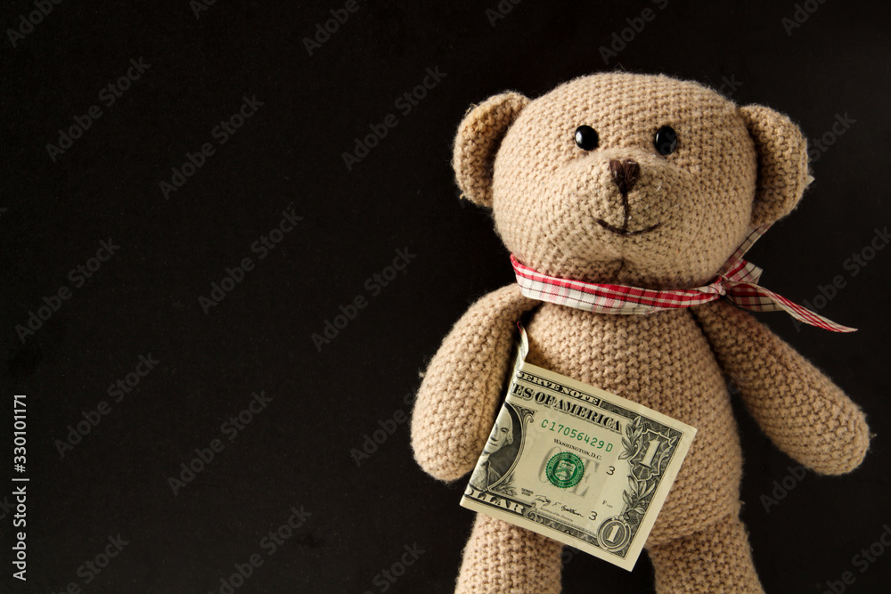 Teddy bear stands and holds money, US dollar, on a black background ...