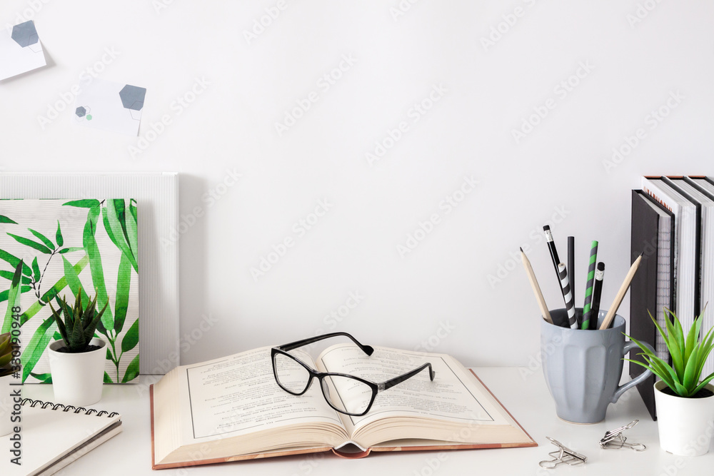 School desk on a white wall. School supplies, mug with pencils, books ...