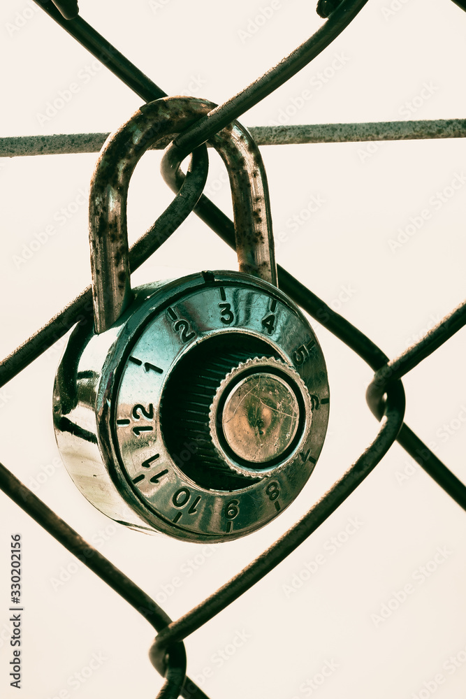 Old round padlock with numbers attached to a fence on white background ...