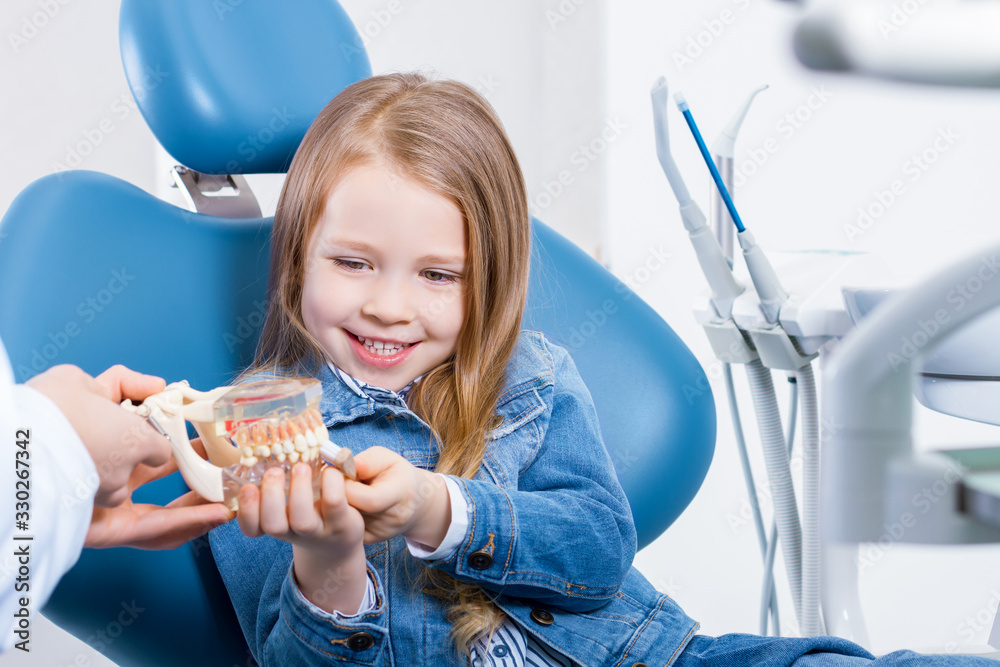 Girl is sitting in dental chair in clinic, office. Woman doctor is ...