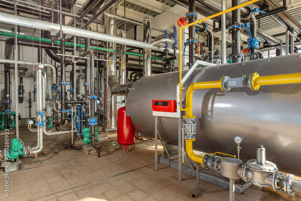 Interior of an industrial boiler room with boilers, many pipes, valves ...