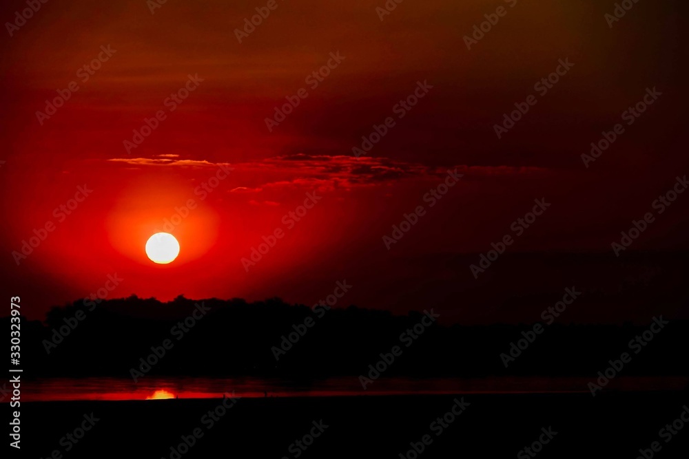 Beautiful scenery of a lake and forest under a red sky with the Sun at ...