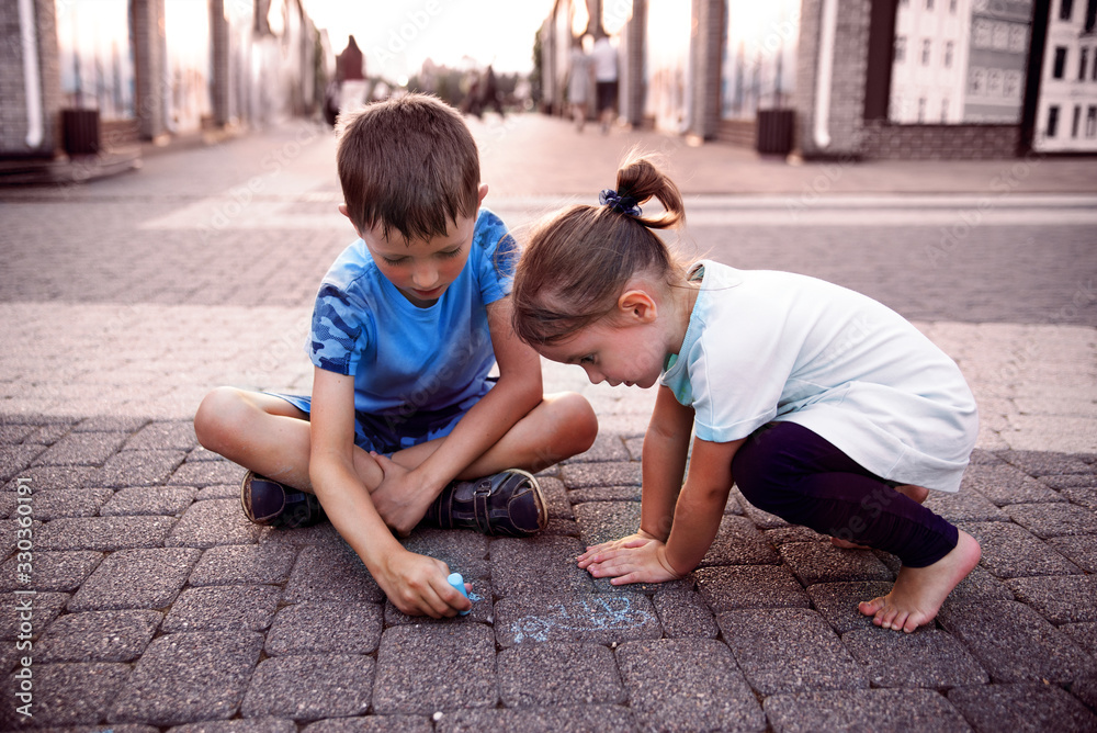 little boy and girl draw on the asphalt with chalk. Happy carefree ...