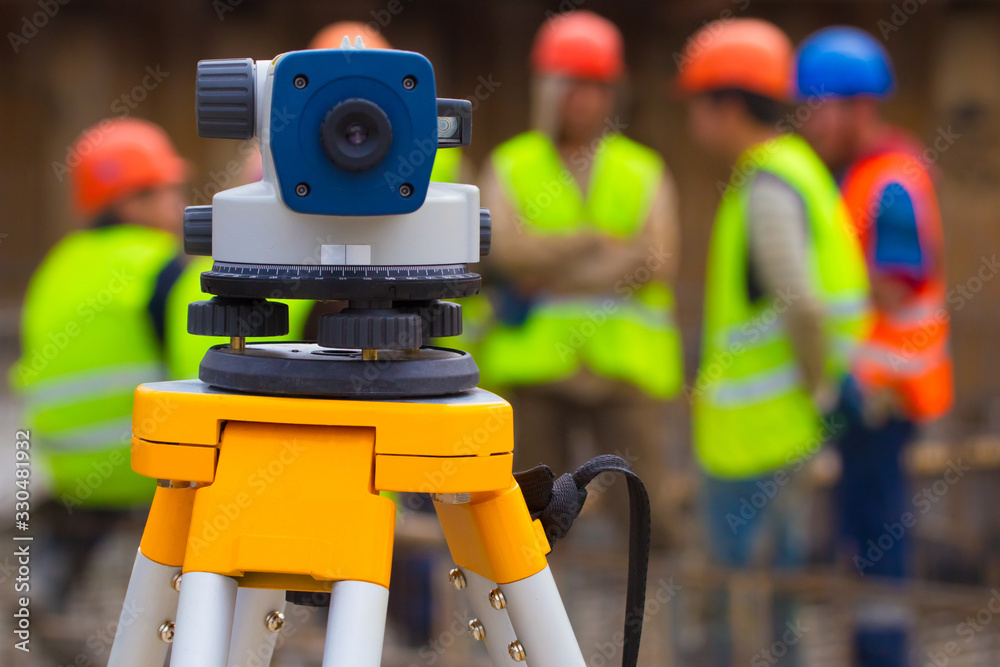 Theodolite on a tripod against the background of Builders in helmets ...