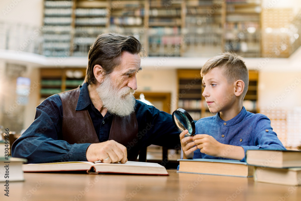 Smart kid boy holds magnifying glass and looking at old man grandfather ...