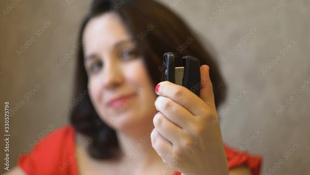 A young woman is sitting indoors. In the hand is a stapler. Happy face ...