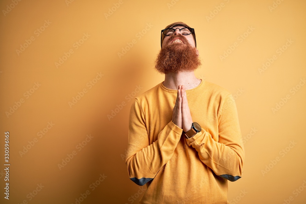 Handsome Irish redhead man with beard wearing glasses over yellow ...