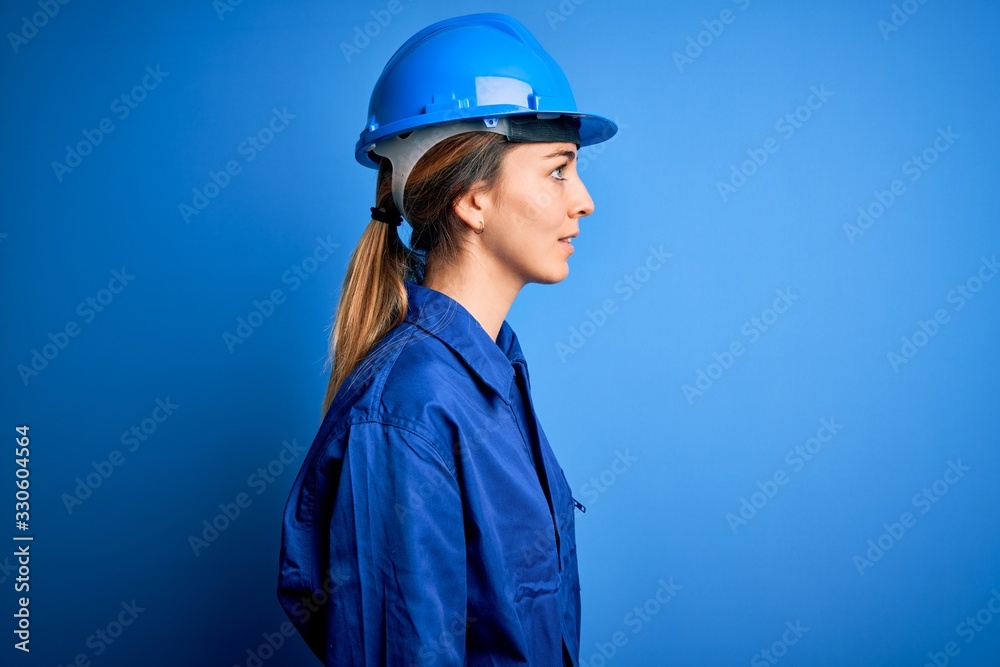 Young beautiful worker woman with blue eyes wearing security helmet and ...
