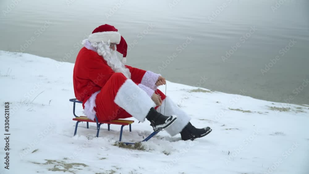 Santa Claus sits in a sled on the snowy shore of the sea, and tries to ...