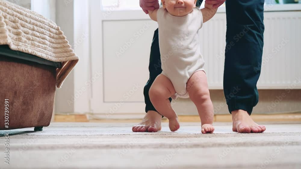 Little baby boy walking barefoot with help of father in home. Baby ...