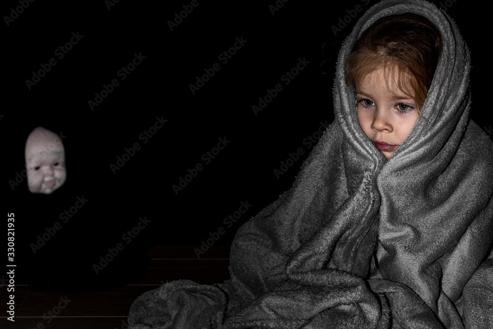 a little girl sitting in the dark wrapped in a blanket, in the ...