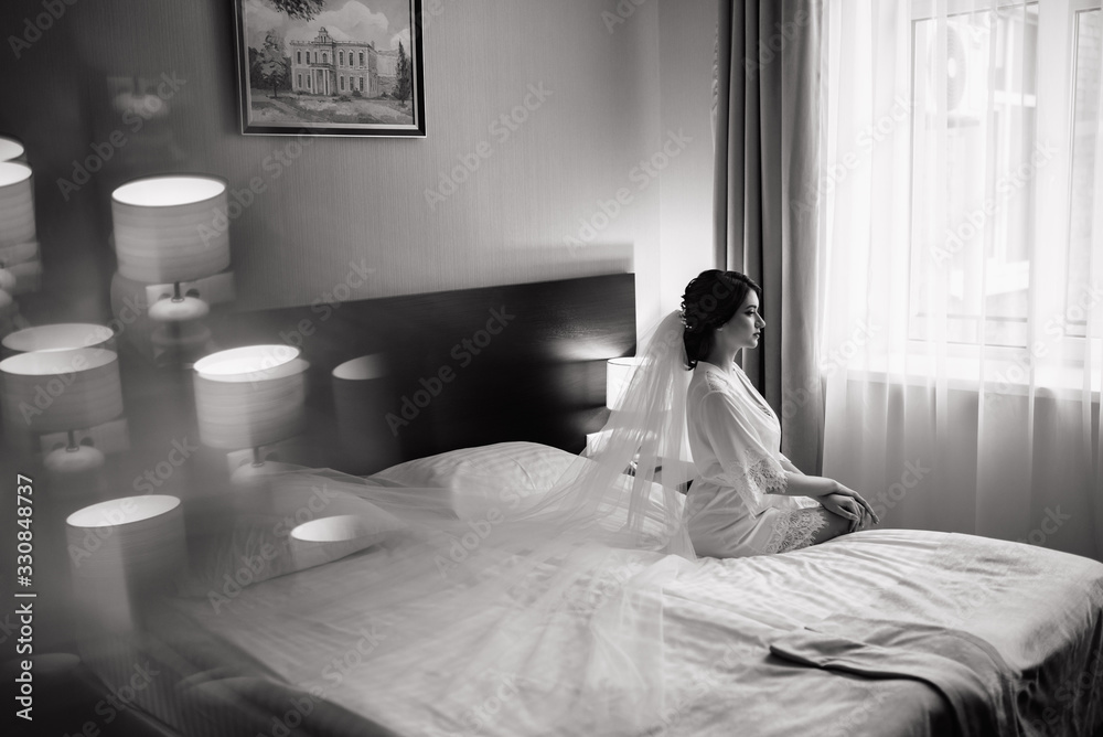Beautiful happy bride sits on a bed. Bride with elegant hairstyle and ...