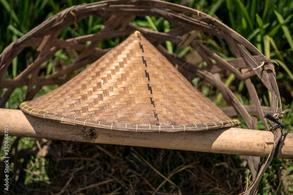 A woven conical rice paddy hat rests on a bamboo pole and wicker basket ...