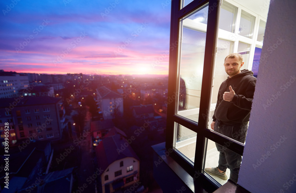 Man is standing on a balcony with panoramic windows and showing a thumb ...