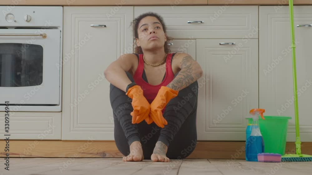 Overworked african american housewife sitting on floor with cleaning ...