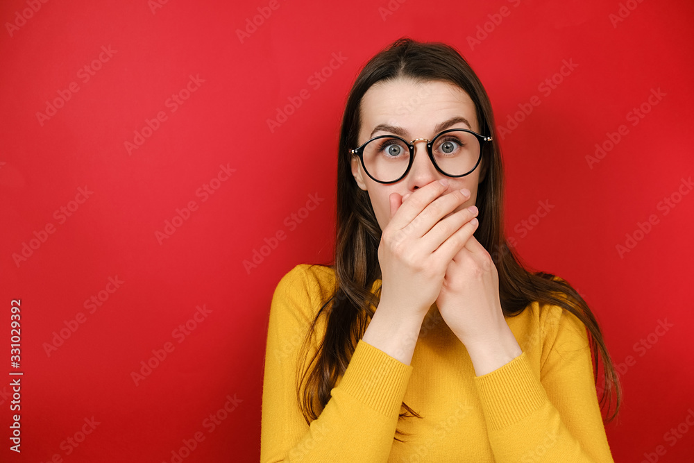Scared woman in eyeglasses looks at camera makes big eyes covering ...