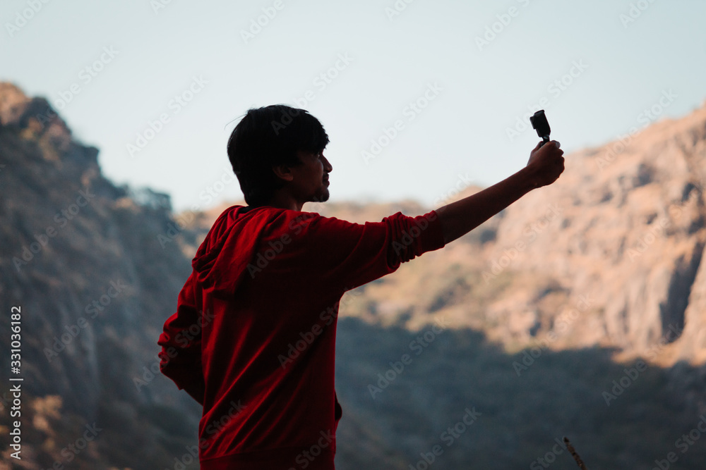 Indian man holding action camera in front of him in front of Mountain ...