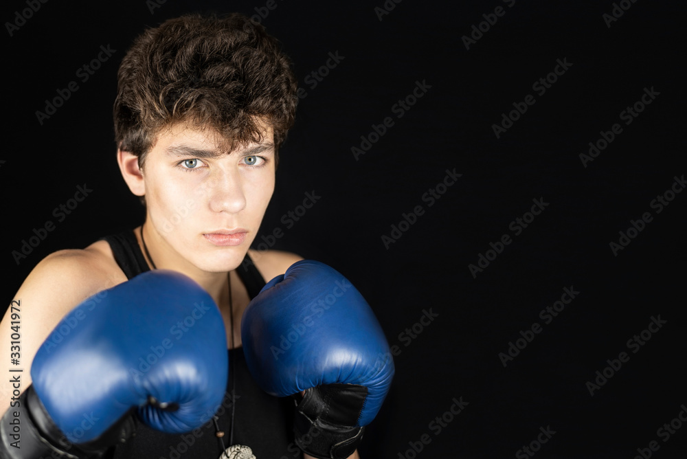 A teenage boy with a serious fighting face in boxing gloves on a dark ...