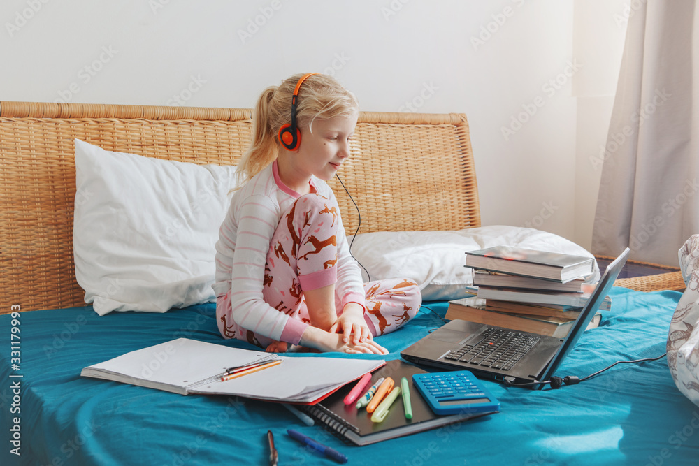 Caucasian girl child sitting in a bed and learning online on laptop ...