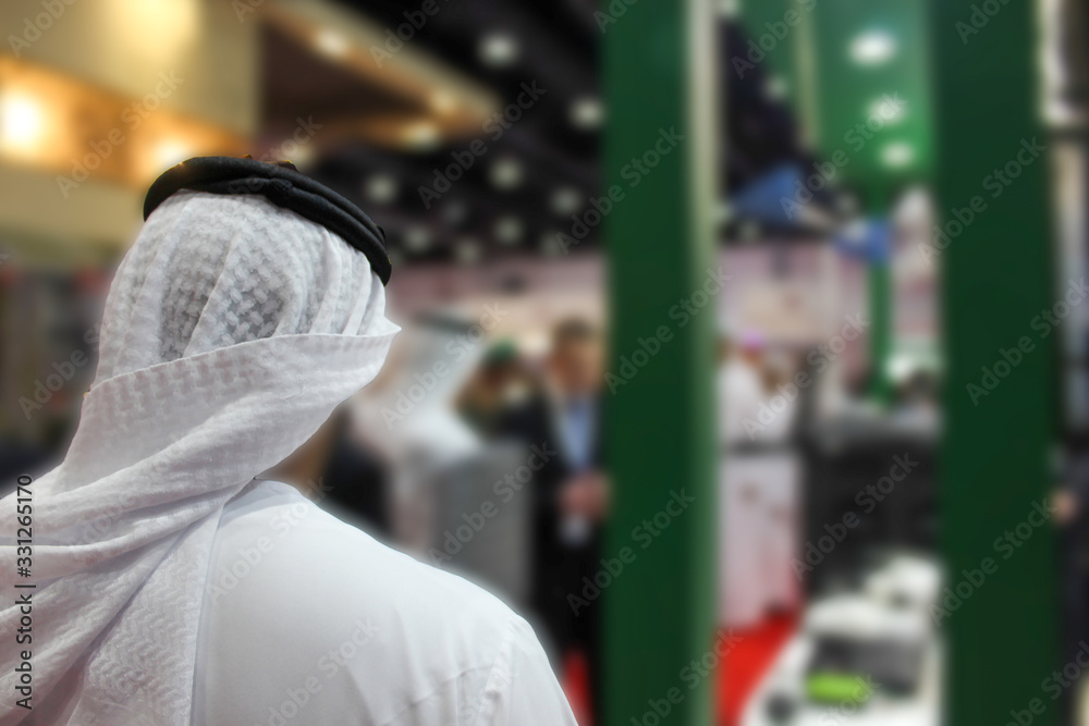 Arab man standing with his back at an exhibition. Blurred background ...