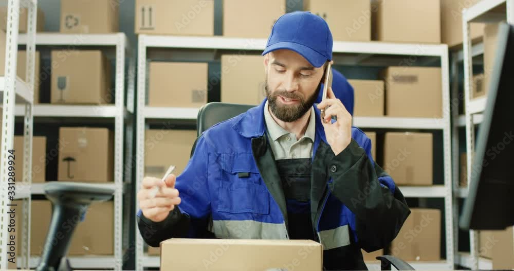 Caucasian postman talking on mobile phone while working at post office ...