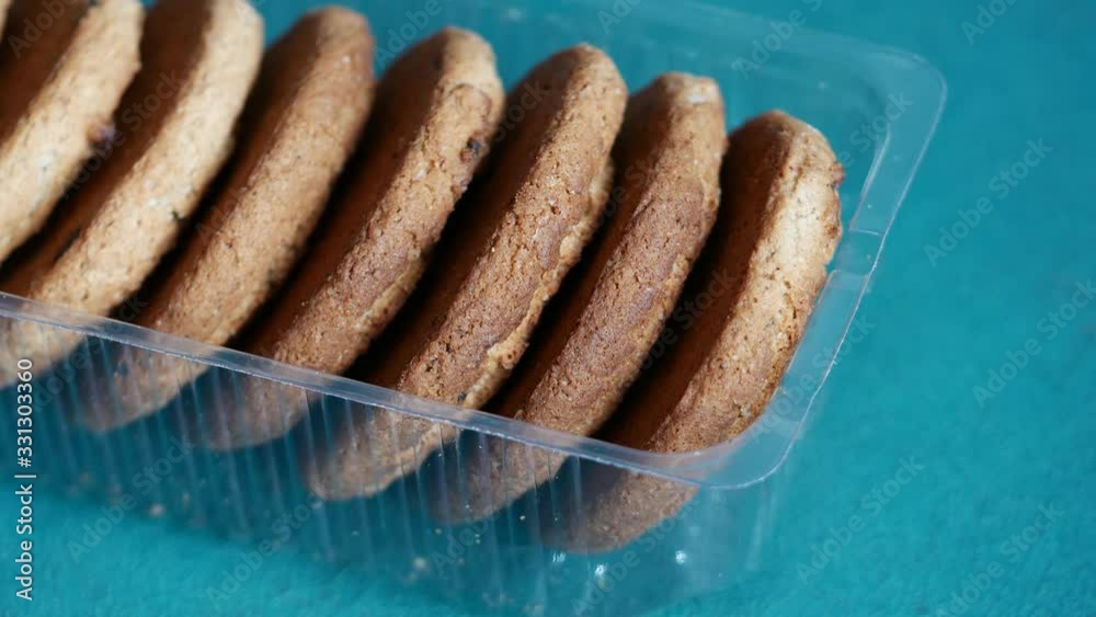 Oatmeal cookies lie in transparent open plastic tray. Male hand takes ...