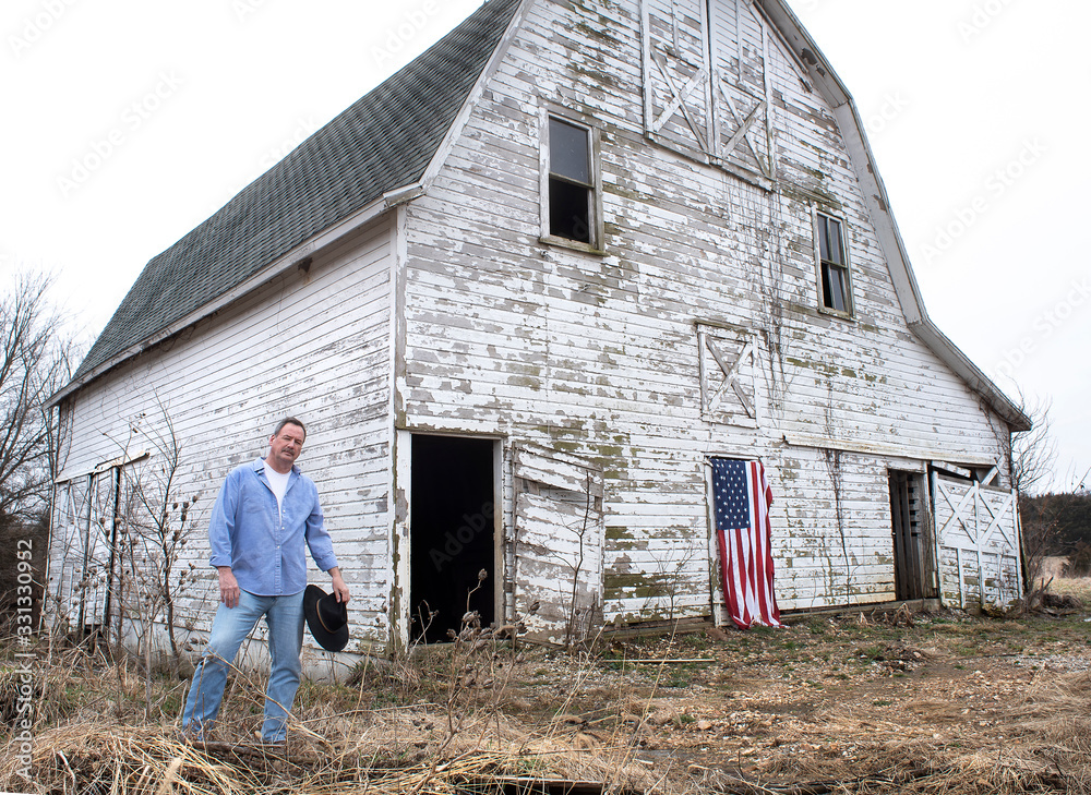 Man with cowboy hat standing in front of old abandoned barn in country ...