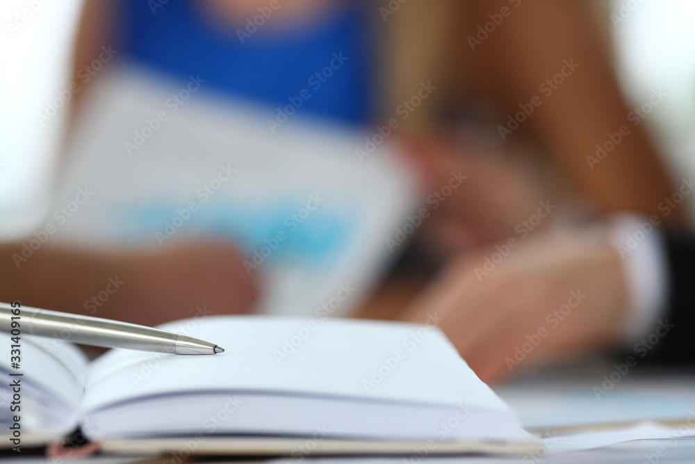 Silver pen lying on opened notebook sheet with people in background in ...