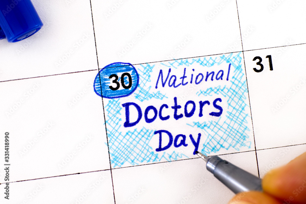 Woman fingers with pen writing reminder National Doctors Day in ...