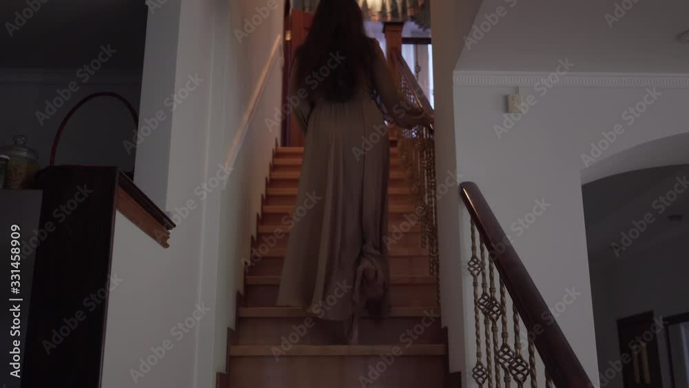 Back view of eerie woman walking up the stairs slowly and entering room ...
