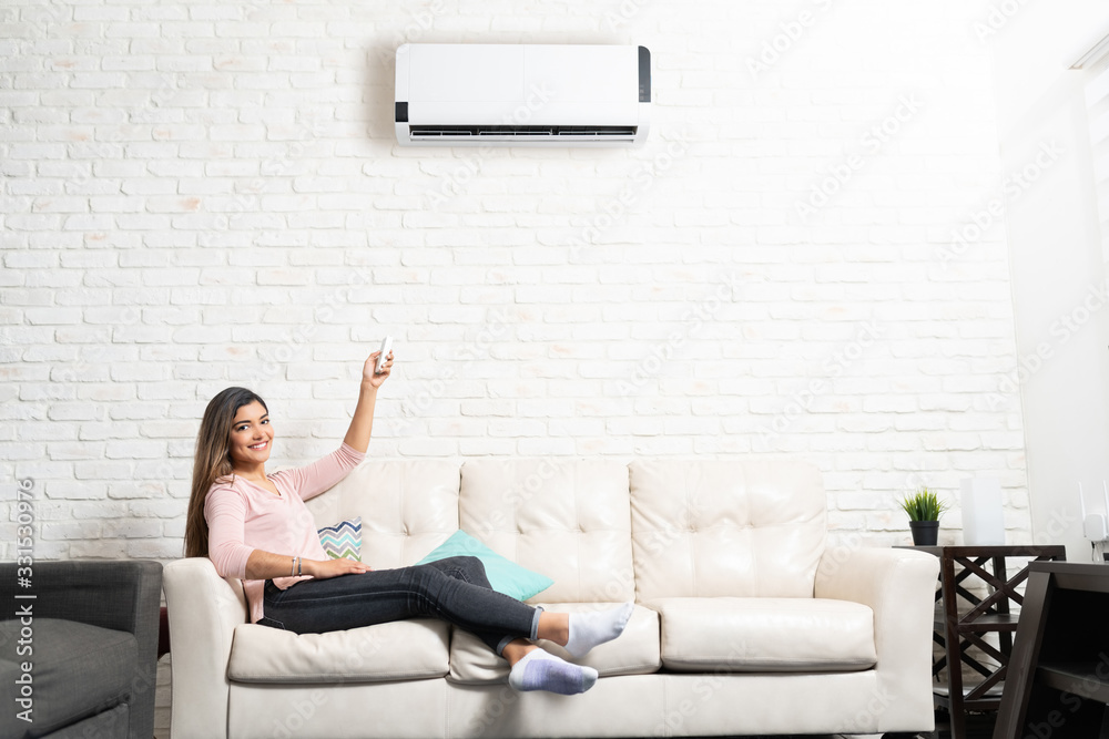 Foto de Smiling Woman Is Adjusting Temperature Of Air Conditioner do Stock | Adobe Stock