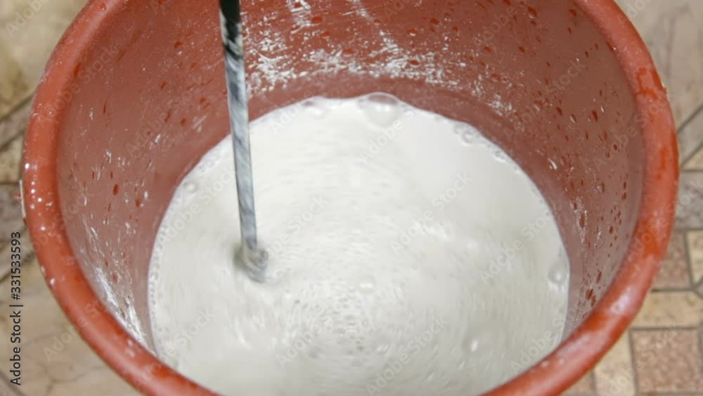 Man knead gypsum plaster in a bucket. Machine mixing gypsum in a bucket ...