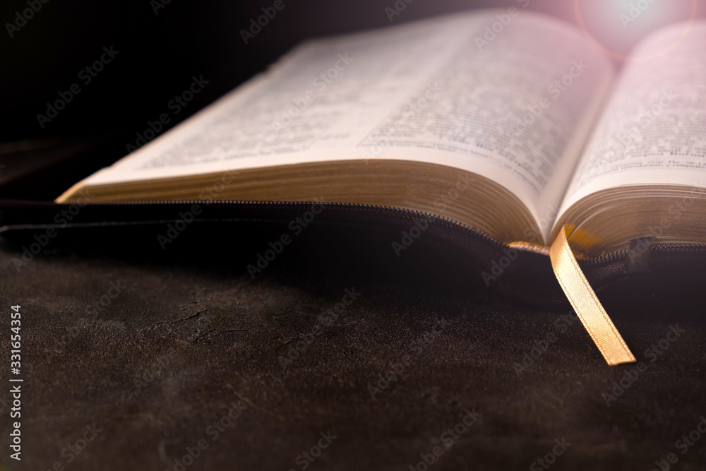 Open Bible on a dark table with light coming from above. Christianity ...