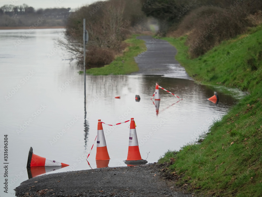 Traffic cone in water during flood by a river. Part of a foot path ...