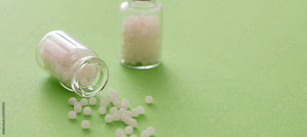 Homeopathy, globules scattered out of glass bottle, green background ...