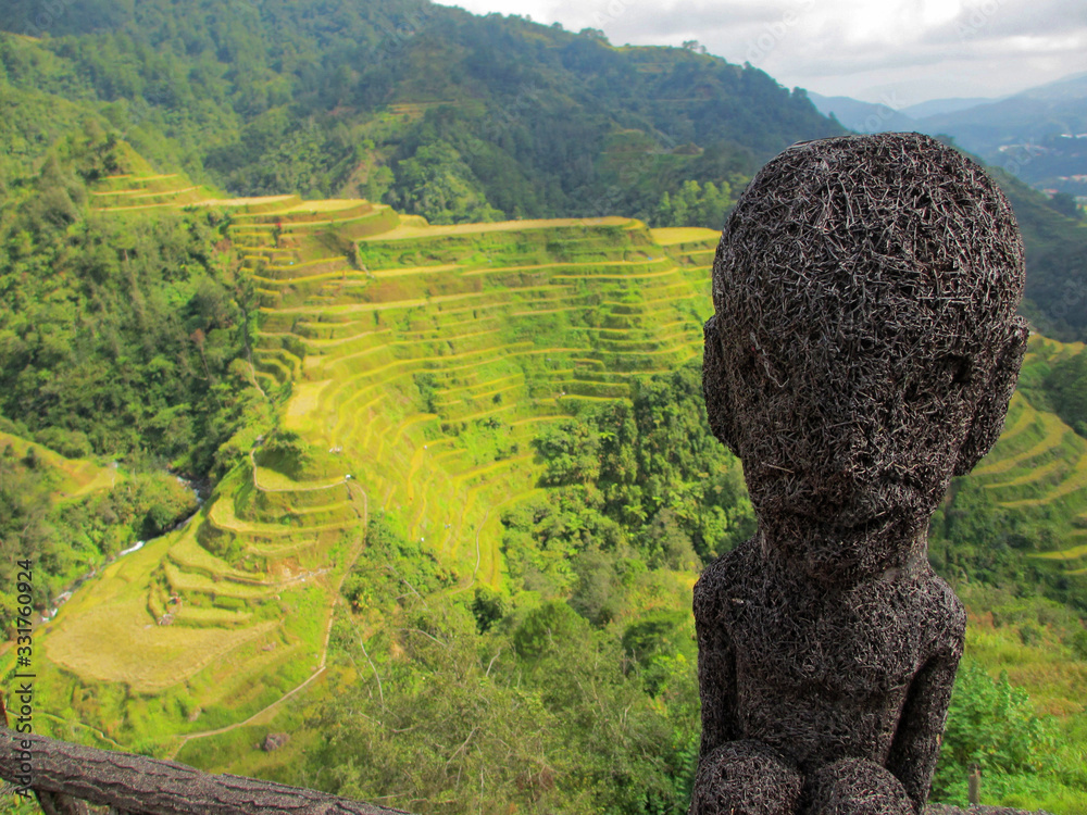 Rice paddy near Banaue in the Philippines with a traditional statue ...