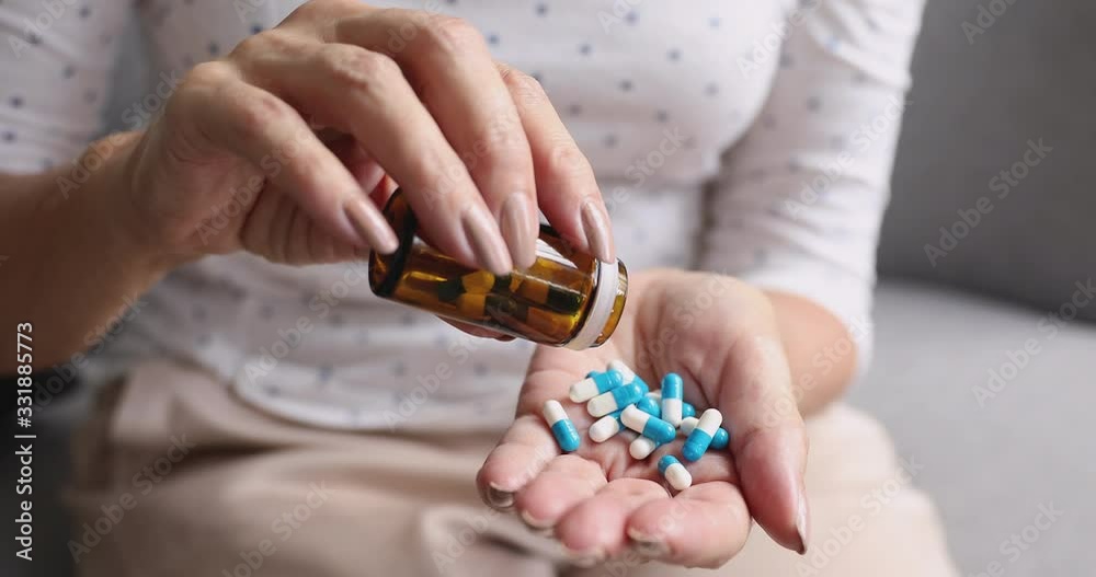 Close up senior woman pouring capsules from glass bottles on hand ...