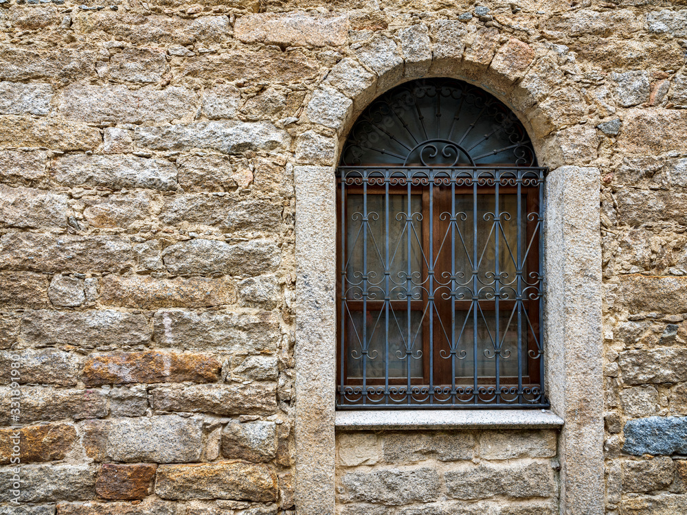 Arched window with wrought iron grate and ancient wall built with ...