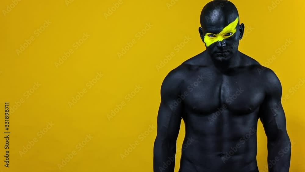 Man bodybuilder athlete with yellow color on face art and black body ...