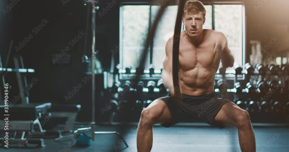 Attractive muscular man working out in the gym using battle ropes with ...