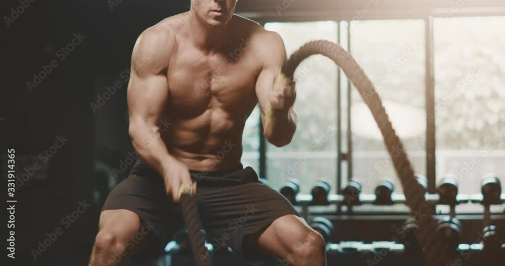 Attractive muscular man working out in the gym using battle ropes with ...