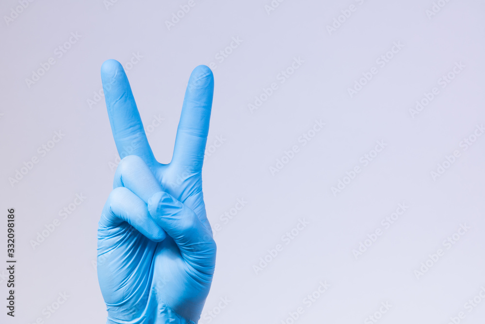 V sign is showed by right man hand in a blue medical glove on a white ...