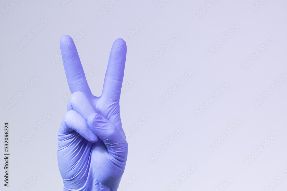 V sign is showed by right man hand in a purple medical glove on a white ...