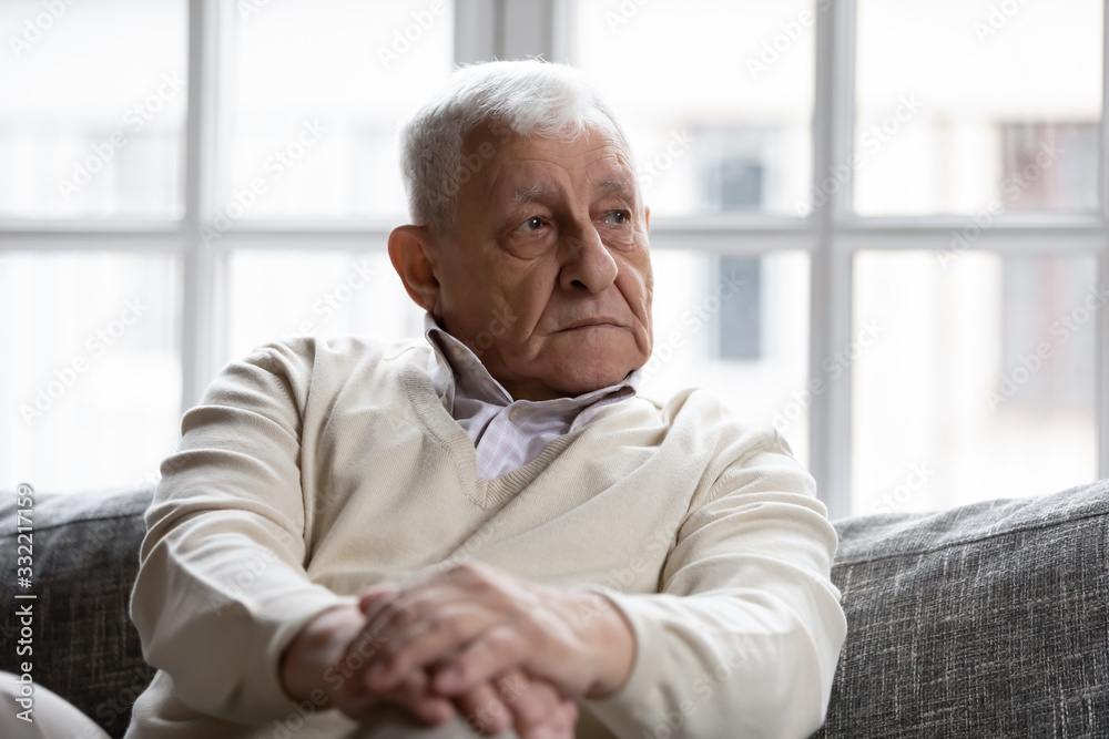 Pensive old man resting at home sitting on couch in living room alone ...